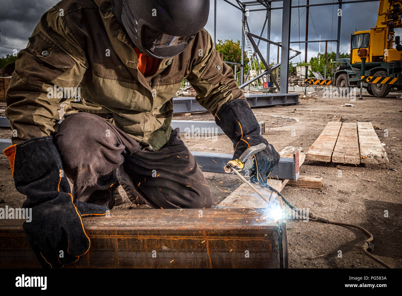 Close up of a strong man is a welder in brown uniform, welding mask and ...