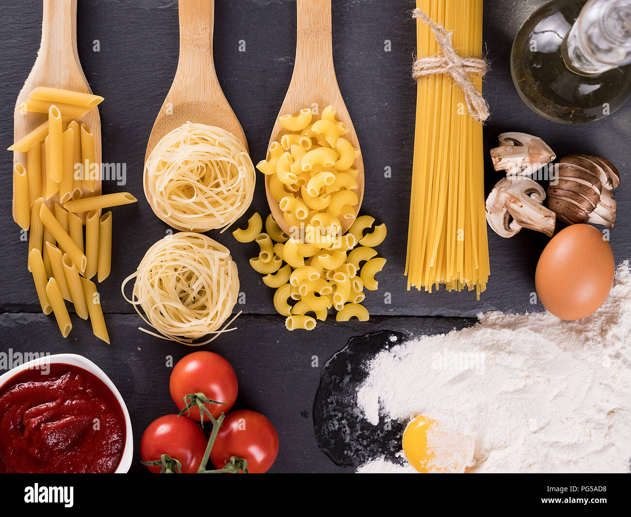 Top view of variety of raw uncooked pasta next to egg in flour, tomato ...