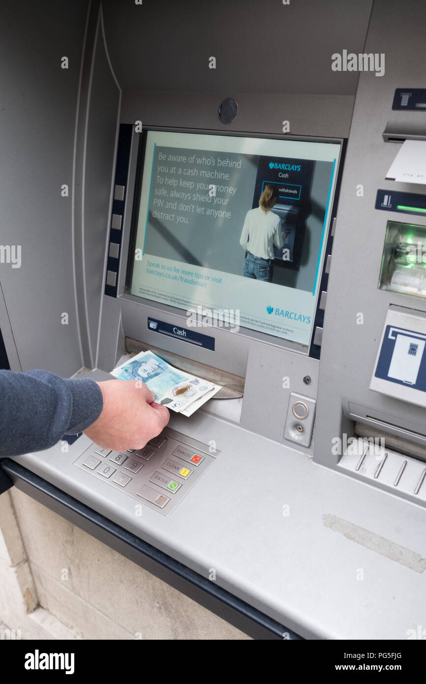 A woman removes £5 and £10 notes from an outside Barclays Bank, hole in ...