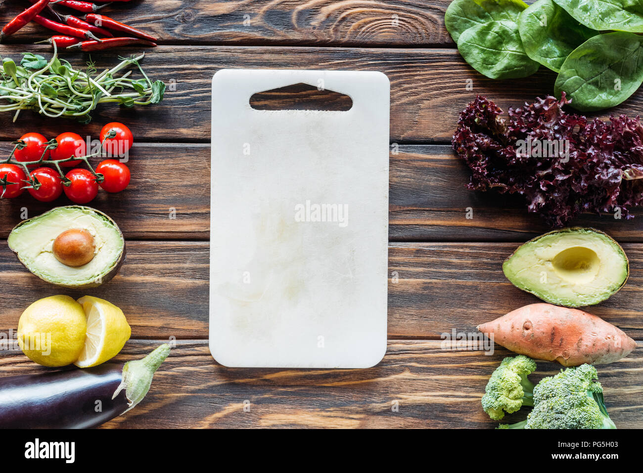flat lay with empty cutting board and fresh vegetables arranged around ...