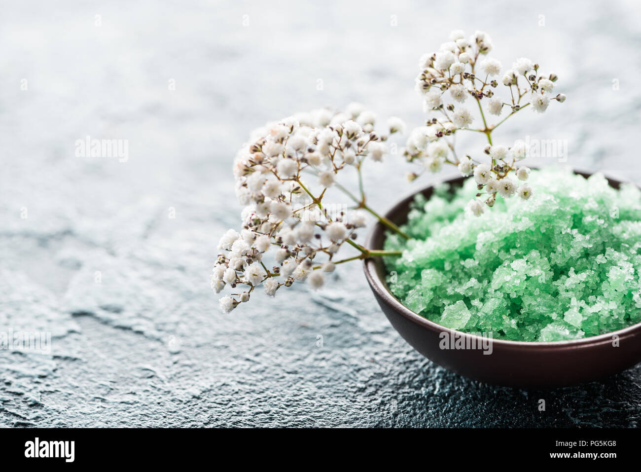 close-up view of green sea salt in bowl and small white flowers ...