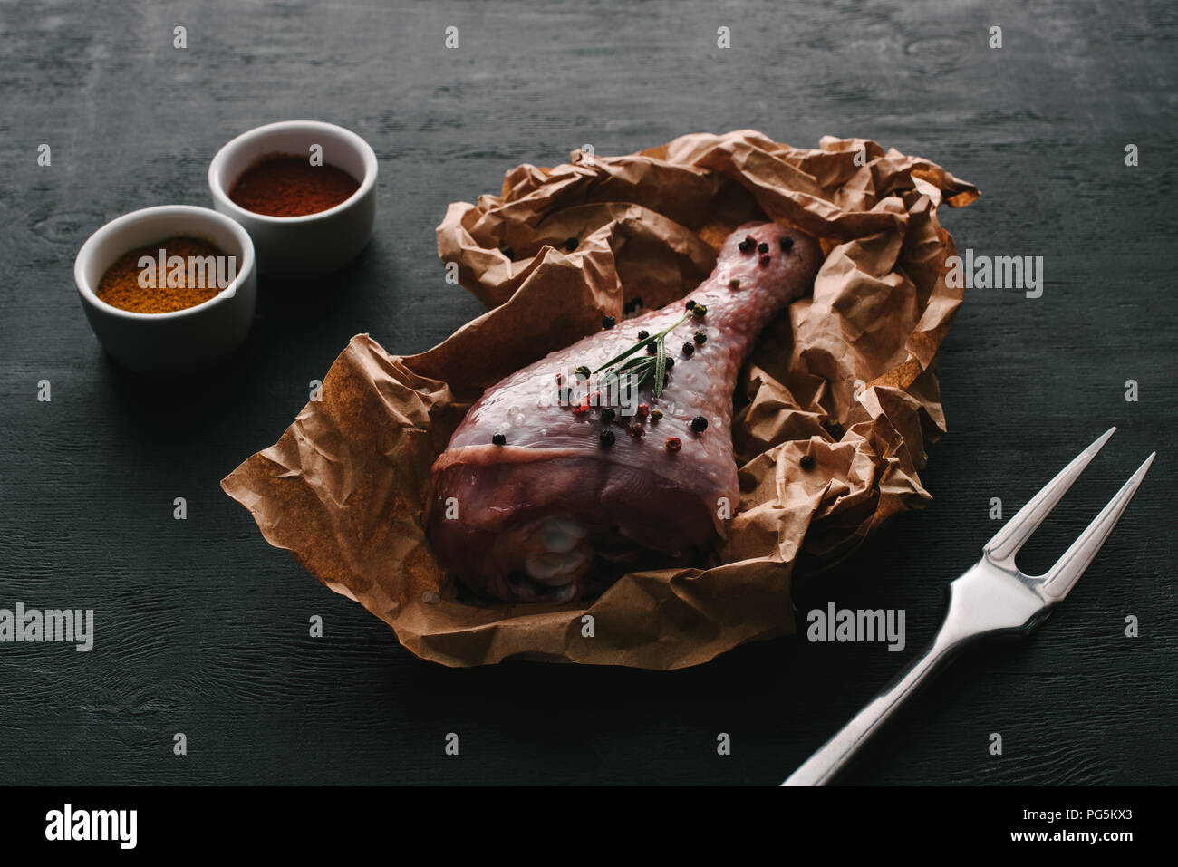 raw turkey leg with pepper corns on baking paper on wooden table with ...