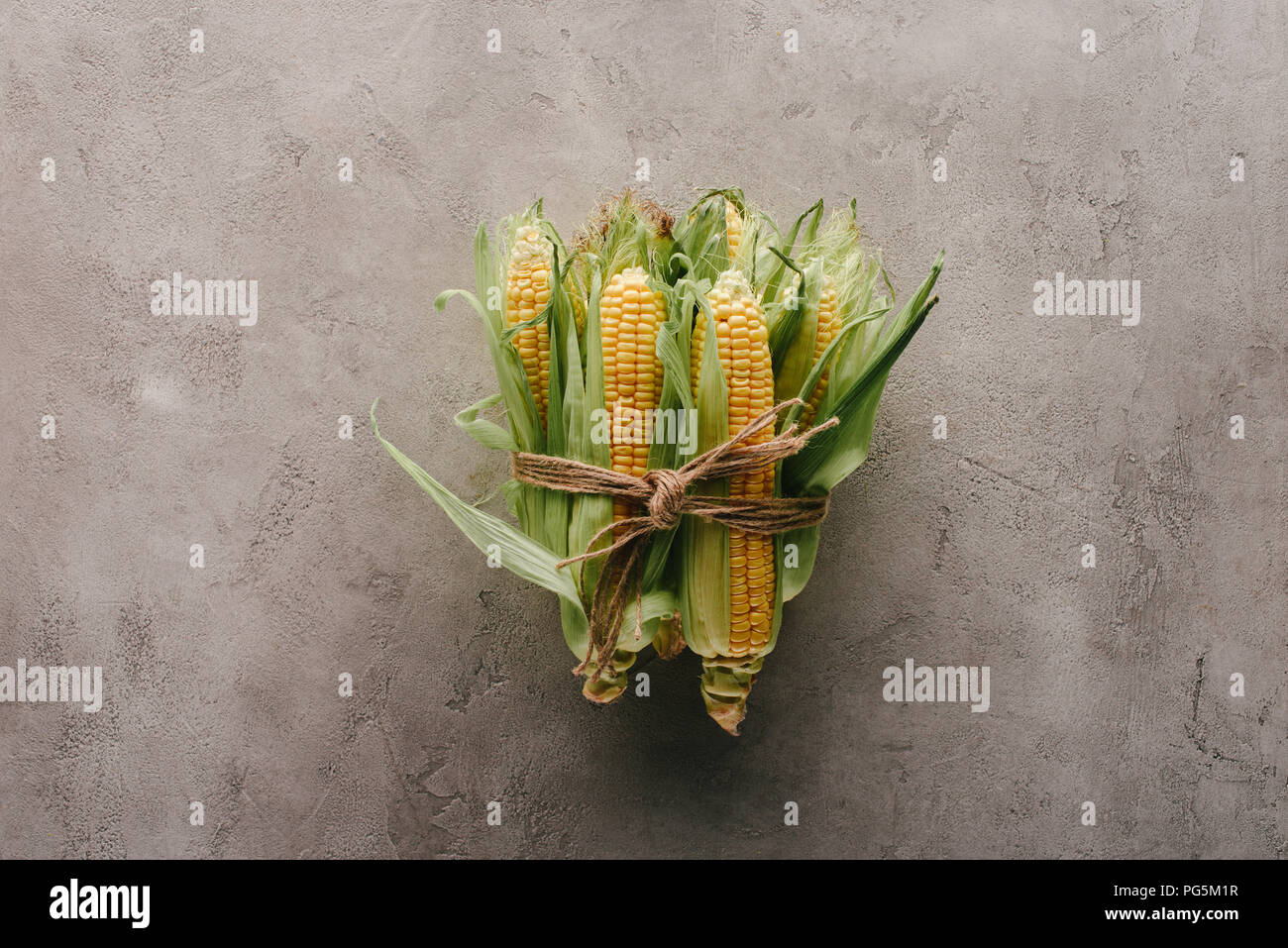 top view of fresh corn cobs tied with rope on grey concrete surface ...