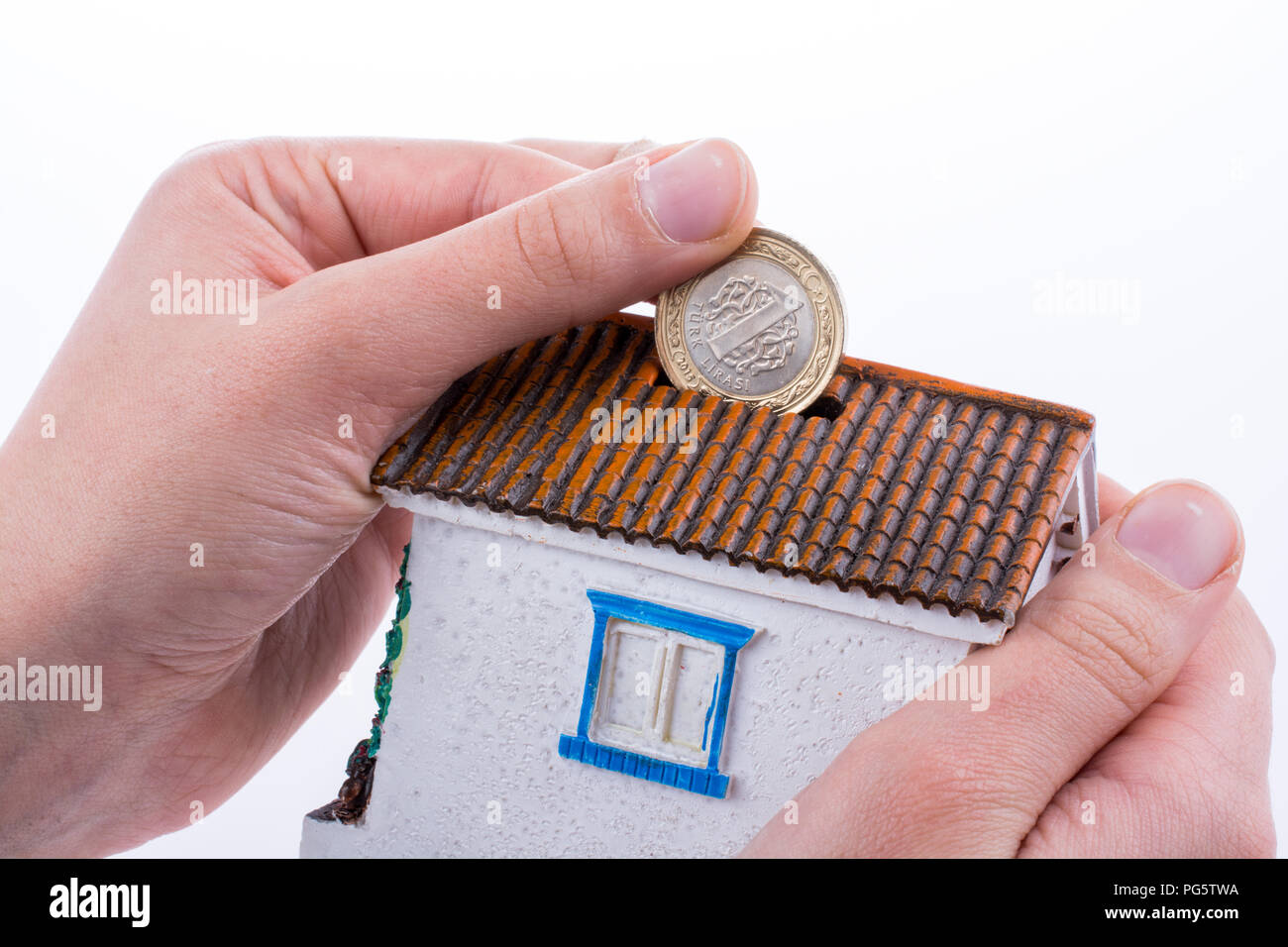 Hand dropping coin into the moneybox in the shape of a model house ...