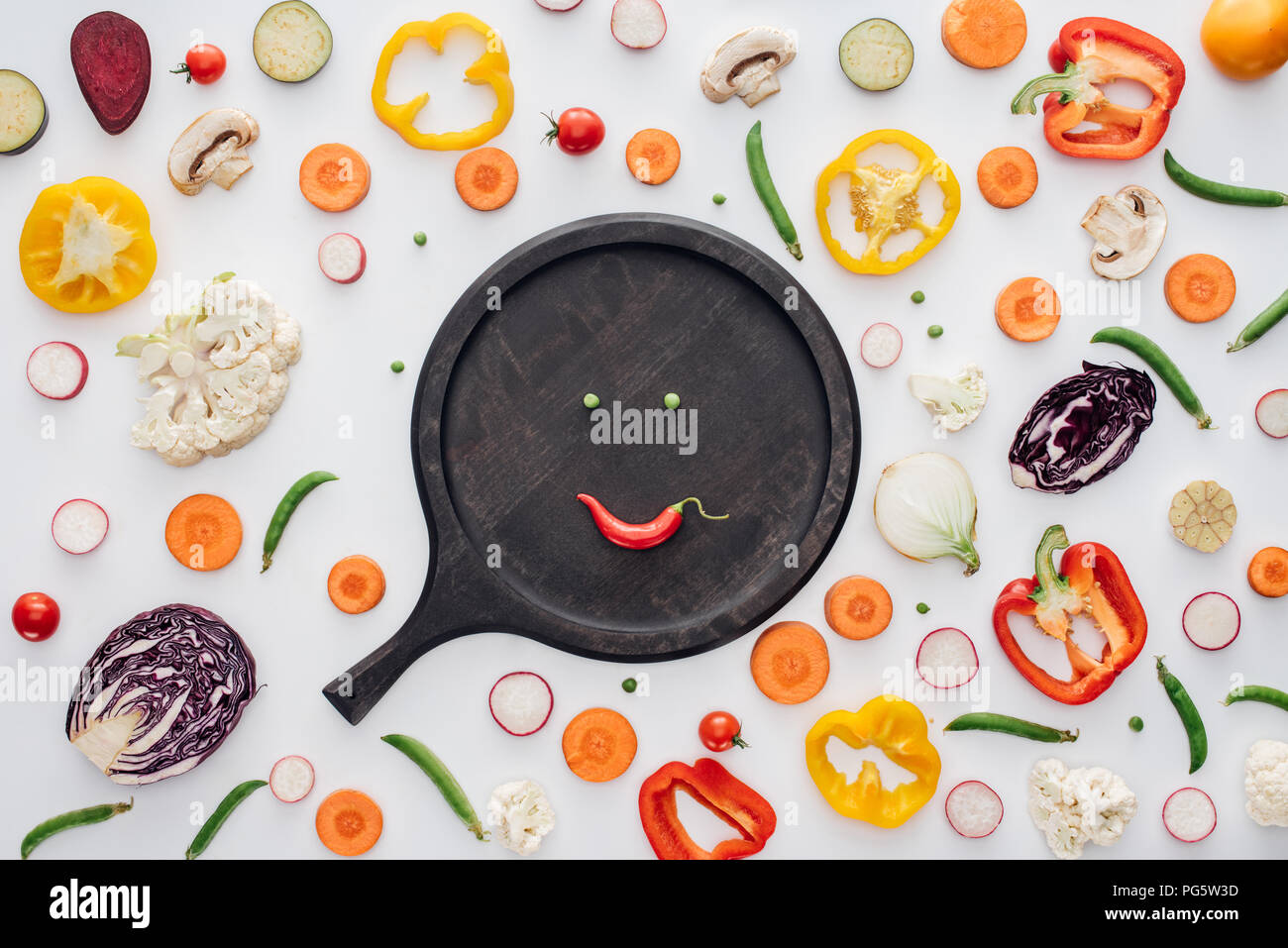 top view of smiley face from green peas and red pepper on round wooden ...