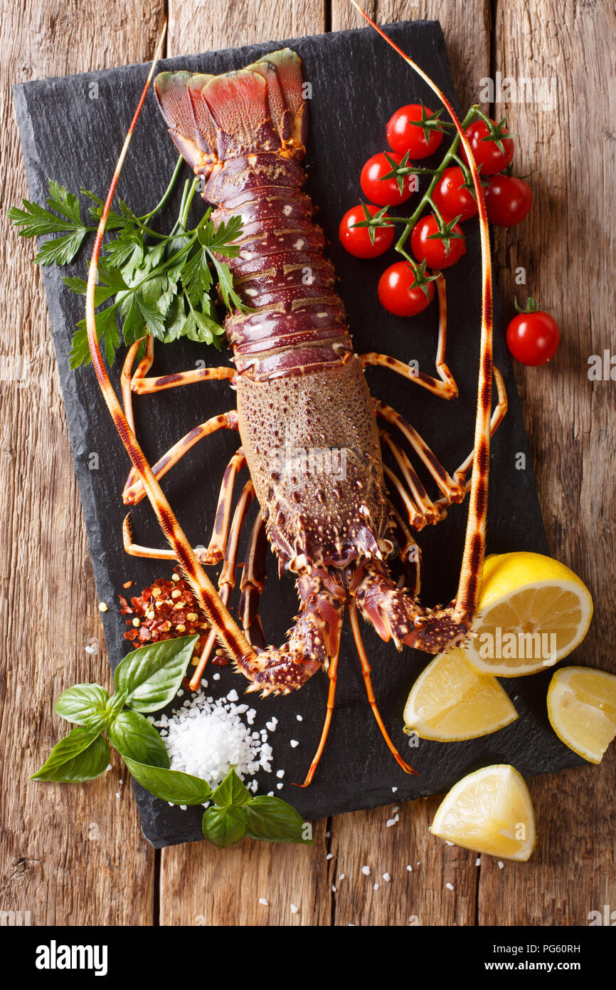 Raw spiny lobster with tomato, lemon and herbs close up on a black ...