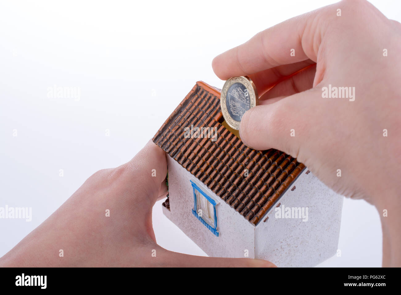 Hand dropping coin into the moneybox in the shape of a model house ...