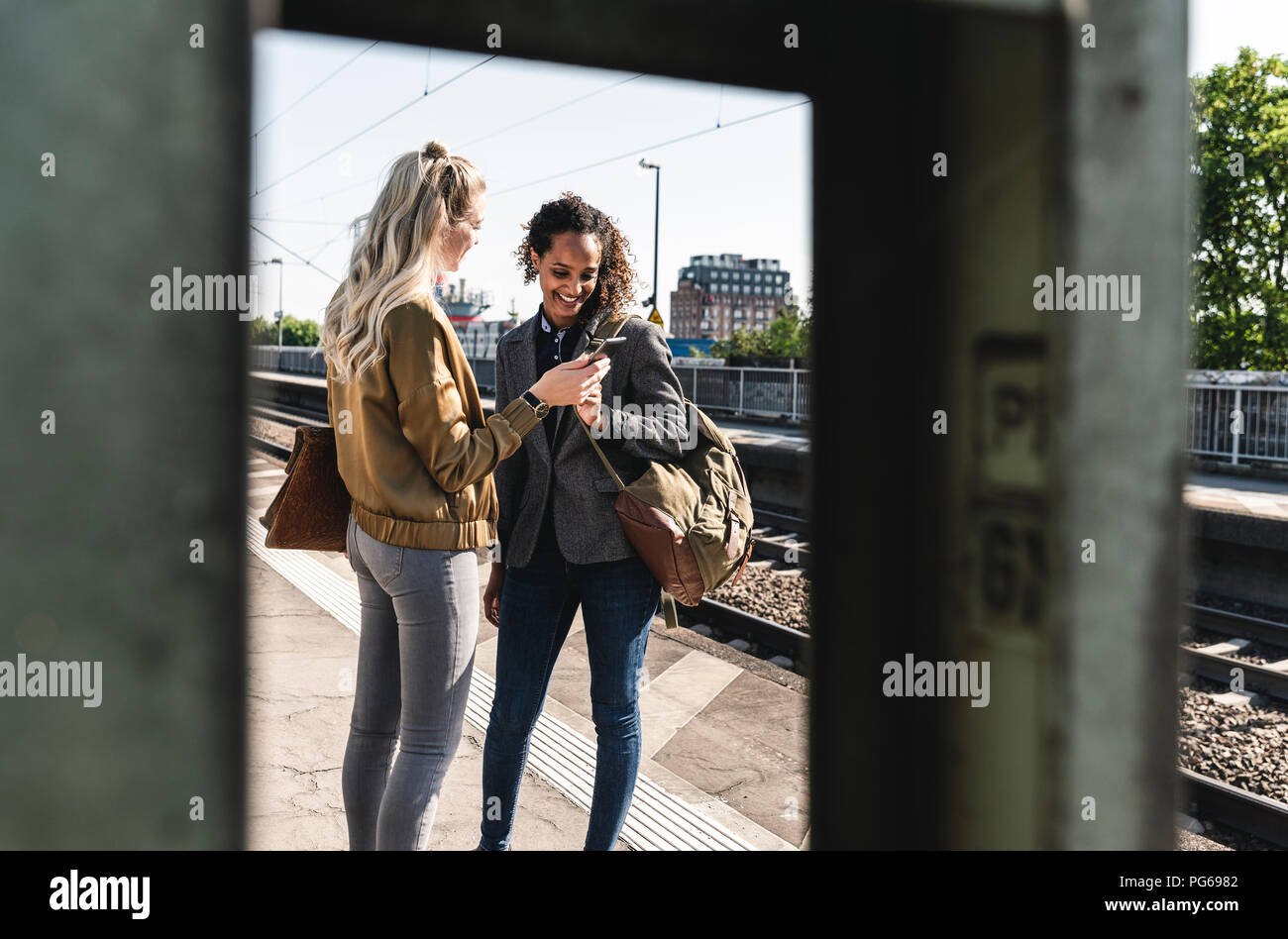 Friends waiting at train station looking at smartphone Stock Photo - Alamy