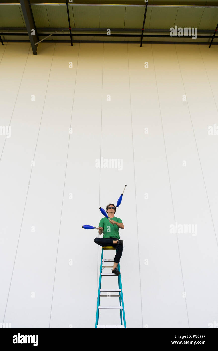 Acrobat wearing sunglasses, sitting on ladder, juggling Stock Photo - Alamy