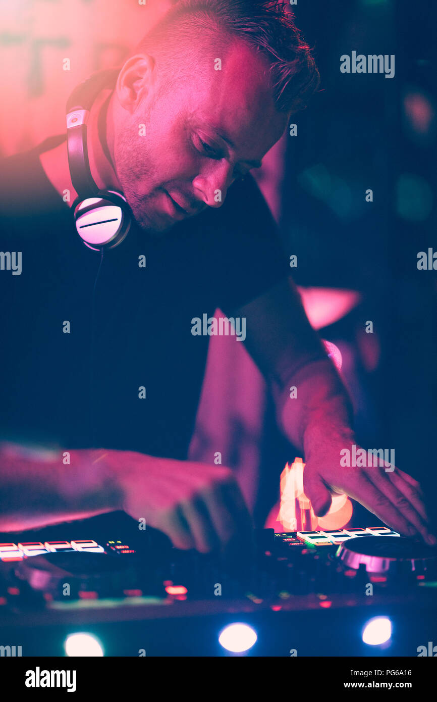 Club, disco DJ playing and mixing music for crowd of happy people ...