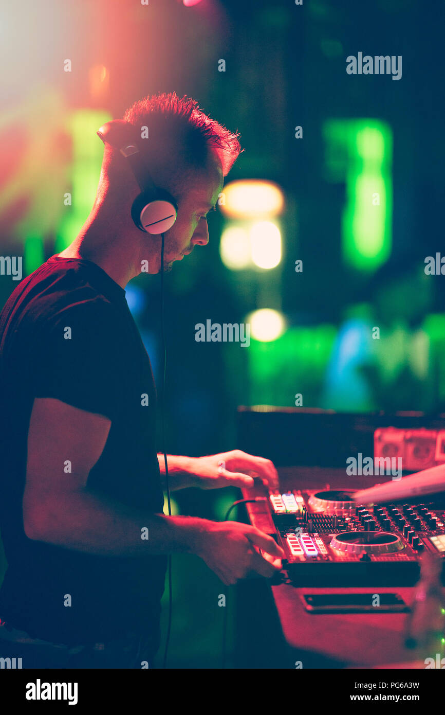 Club, disco DJ playing and mixing music for crowd of happy people ...