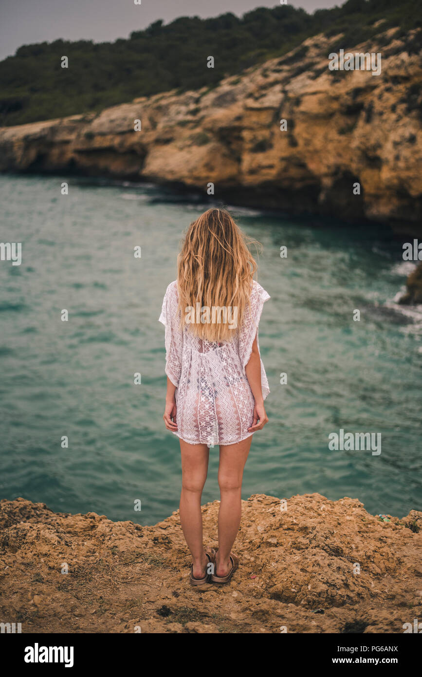 Rear view of young woman standing on a rock at the coast Stock Photo ...