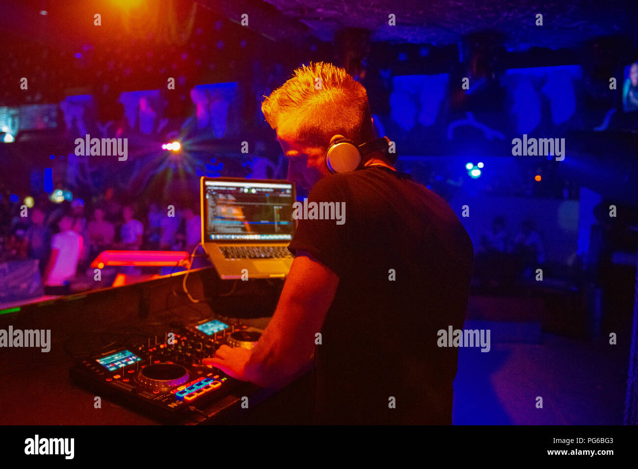 Club, disco DJ playing and mixing music for crowd of happy people ...