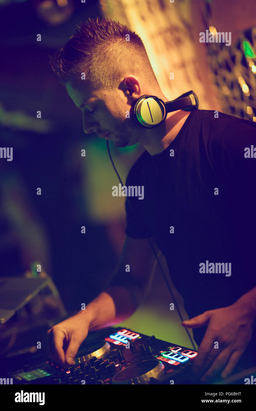 Club, disco DJ playing and mixing music for crowd of happy people ...