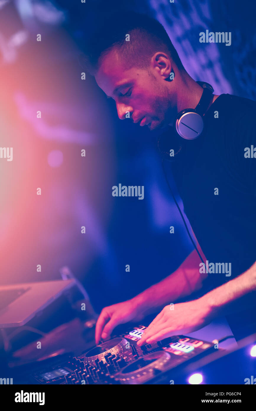 Club, disco DJ playing and mixing music for crowd of happy people ...