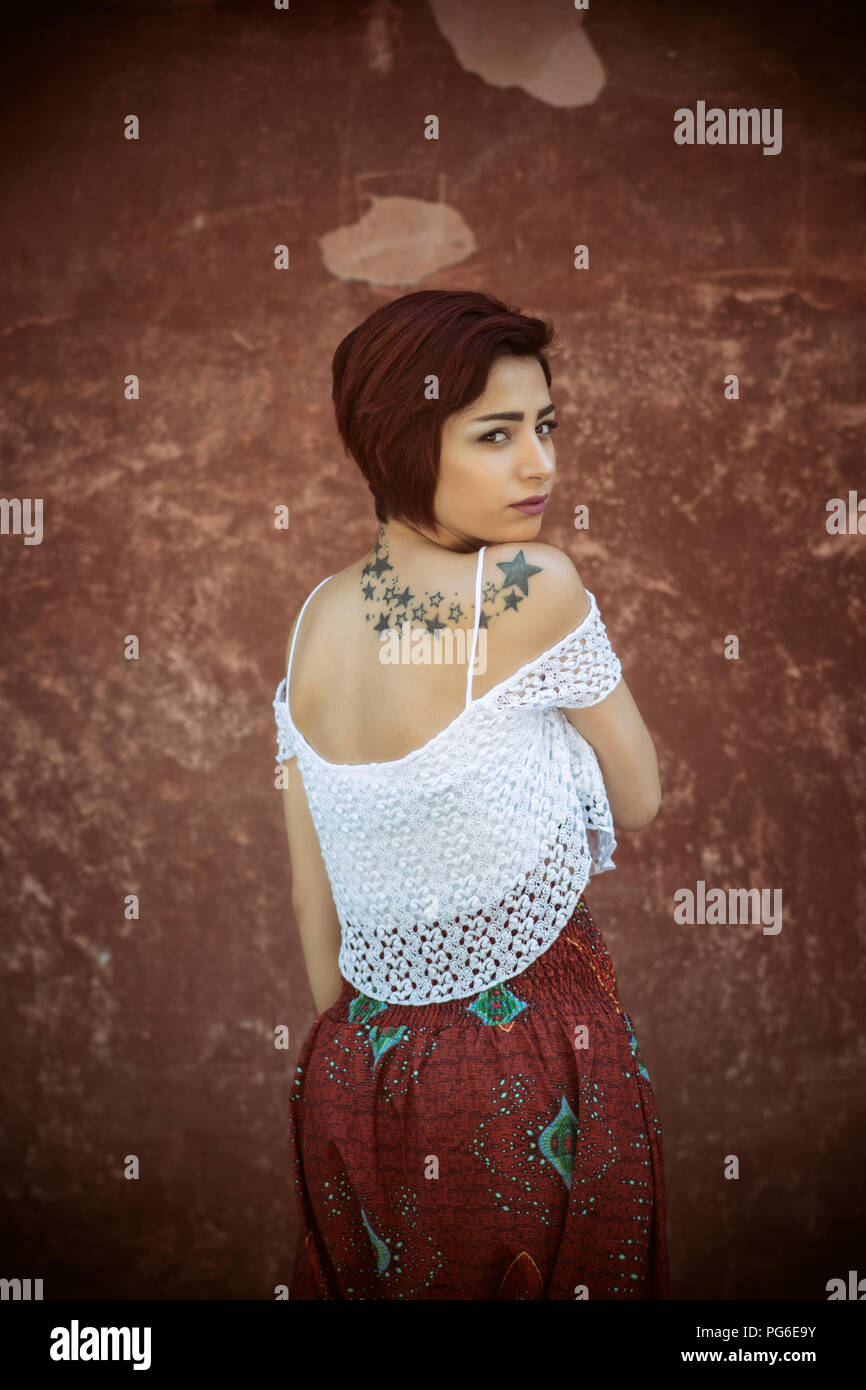 Scared young woman with short red hair looking over shoulder outdoors ...