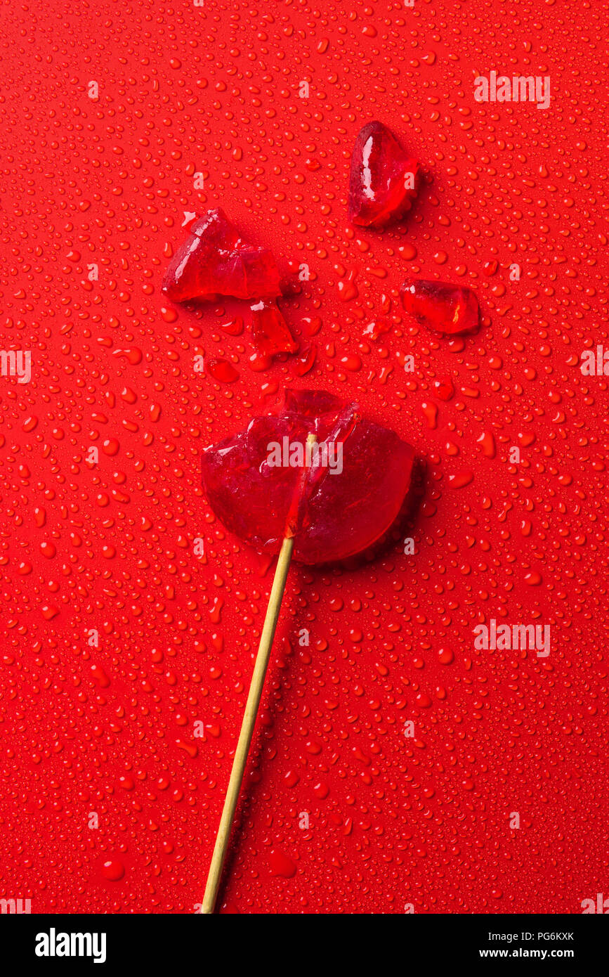 top view of broken lollipop on red surface with water drops Stock Photo ...