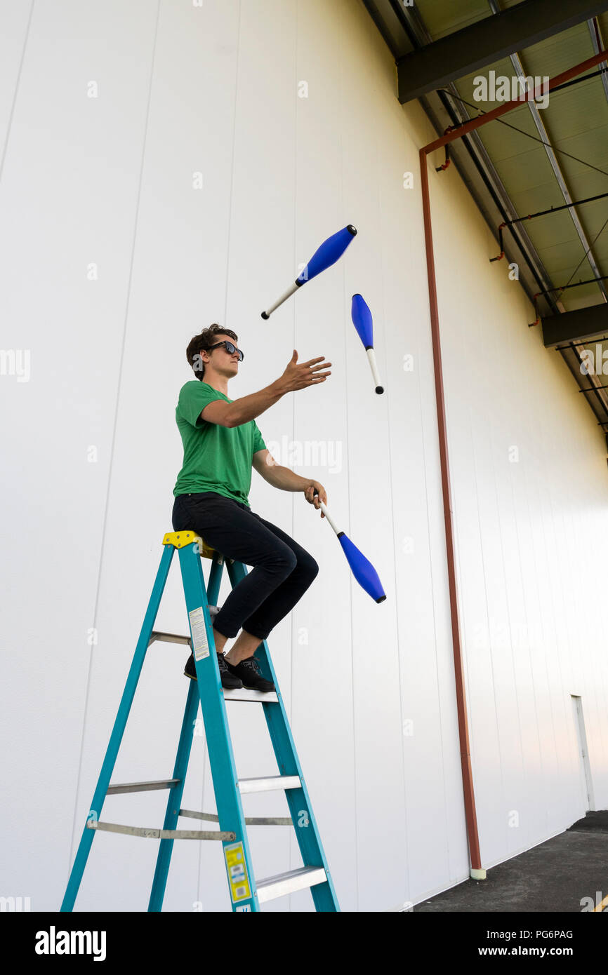 Acrobat wearing sunglasses, sitting on ladder, juggling Stock Photo - Alamy