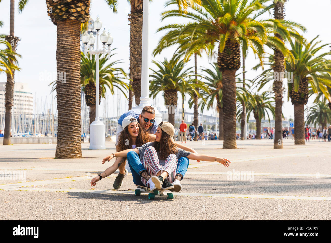 Carefree friends having fun with a skateboard on a promenade with palms ...