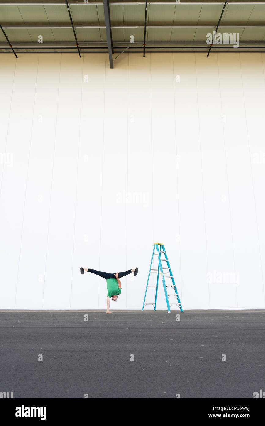 Acrobat training one-armed handstand next to ladder Stock Photo - Alamy