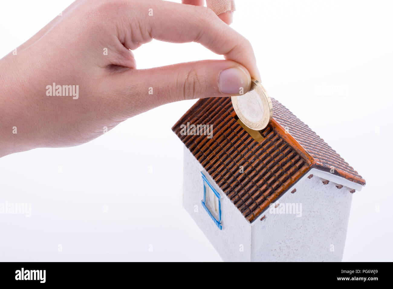 Hand dropping coin into the moneybox in the shape of a model house ...
