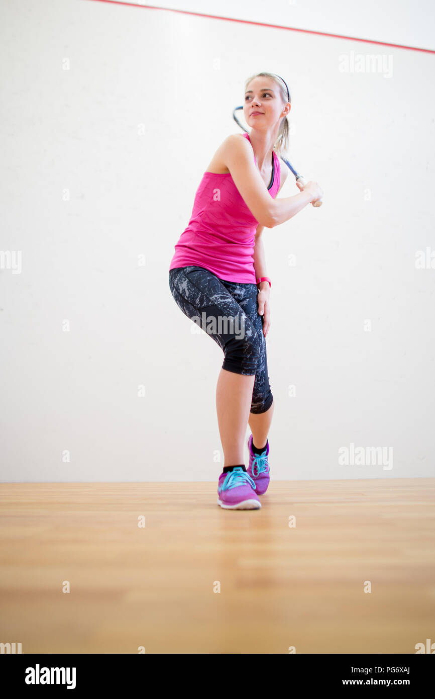 Cute young woman with a racket leaning against a wall in a squash court ...