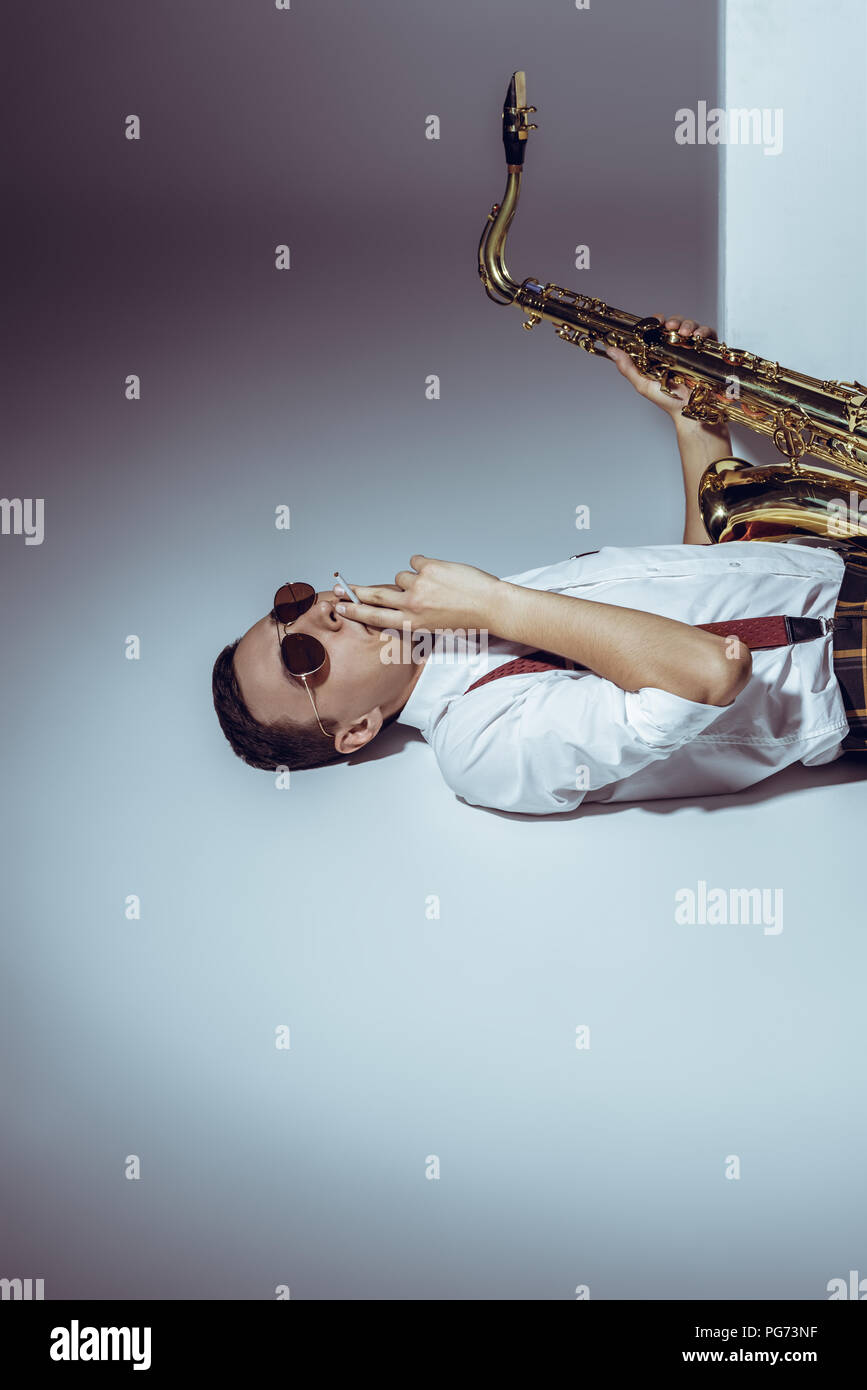 young musician in sunglasses holding saxophone and smoking cigarette ...