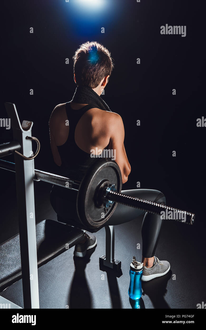 rear view of sportswoman with towel over neck resting near barbell at ...