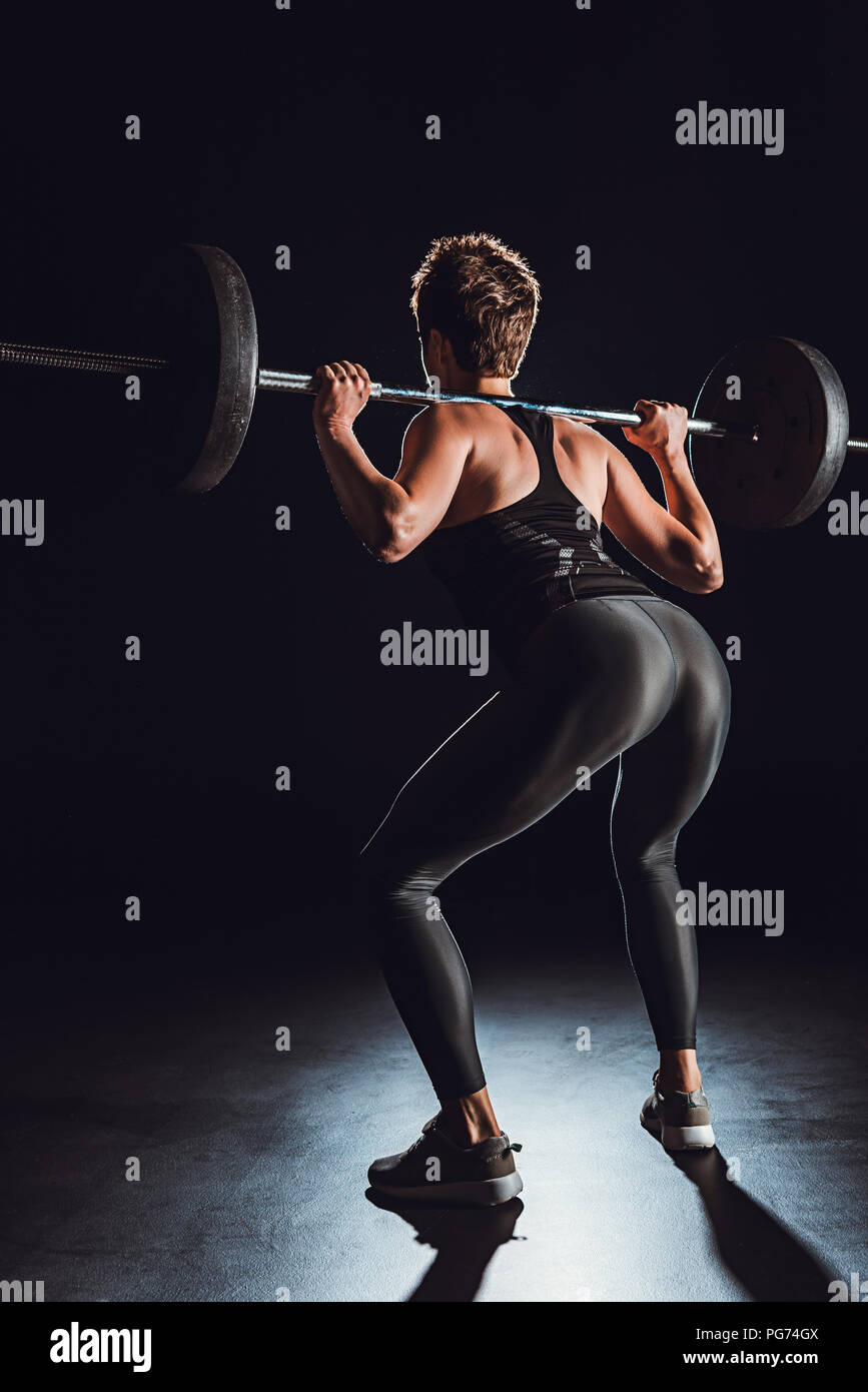 rear view of female athlete doing exercise with barbell, black ...