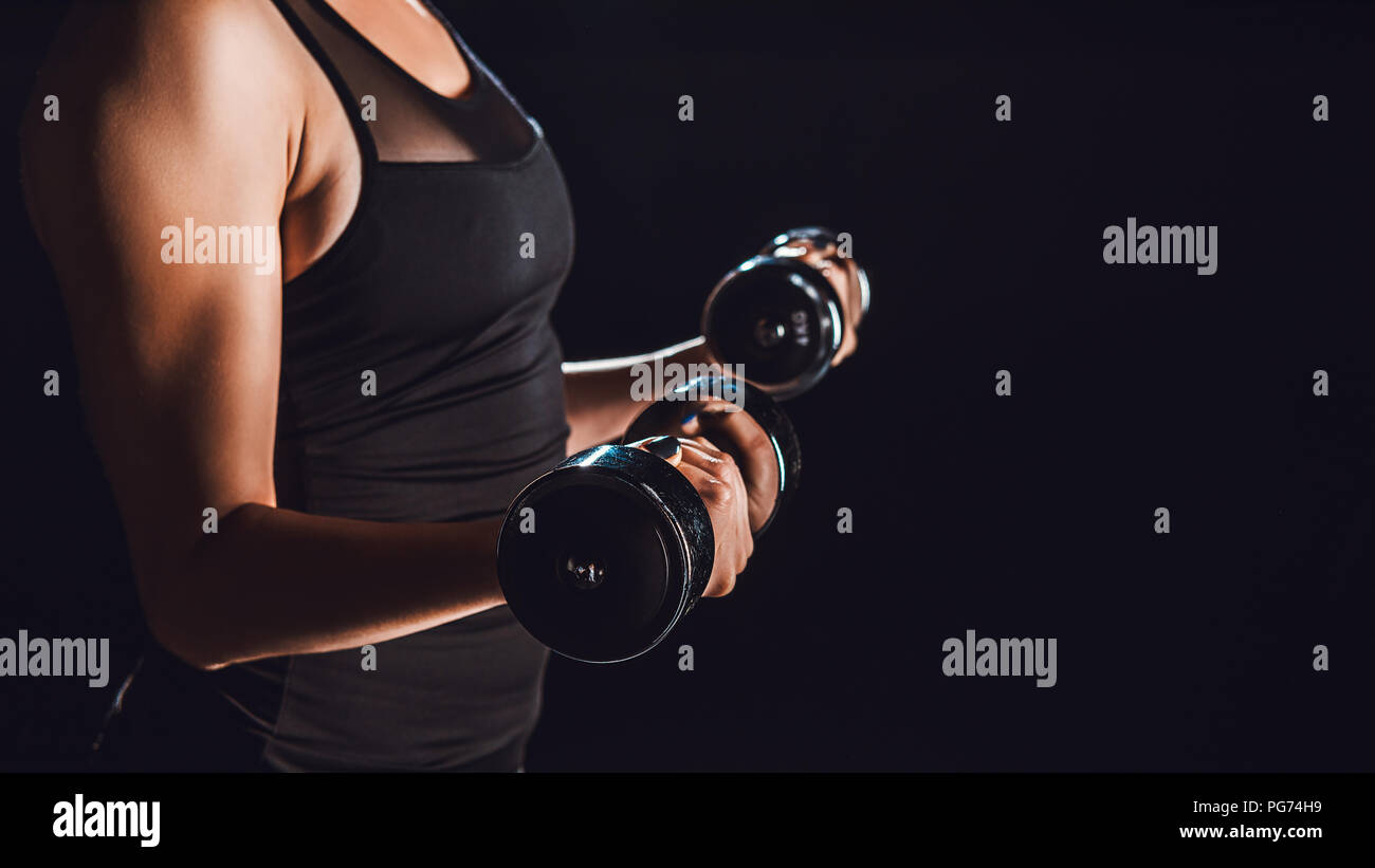 partial view of female bodybuilder working out with dumbbells, black ...