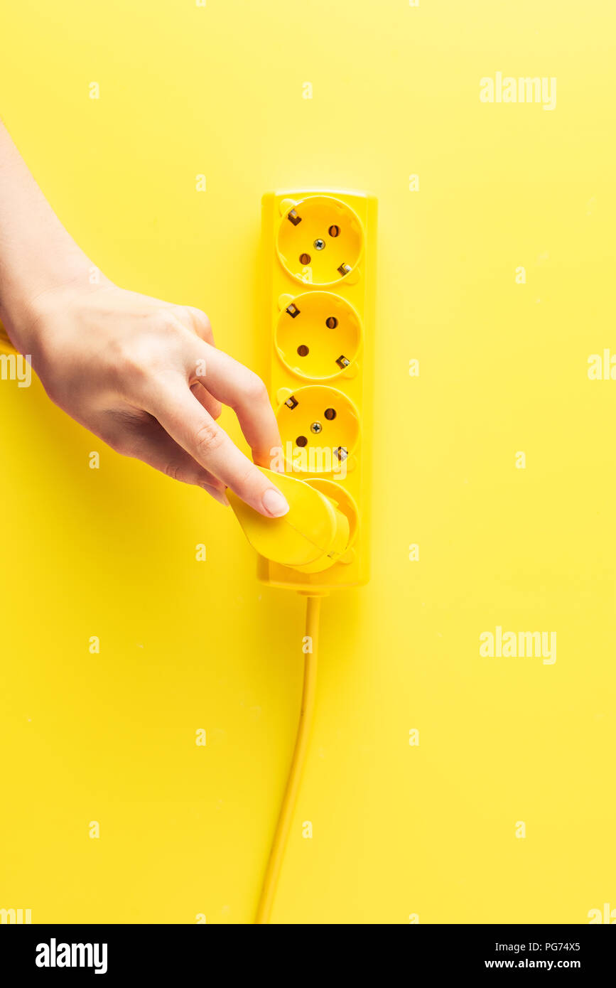 cropped shot of person inserting plug into socket outlet on yellow ...
