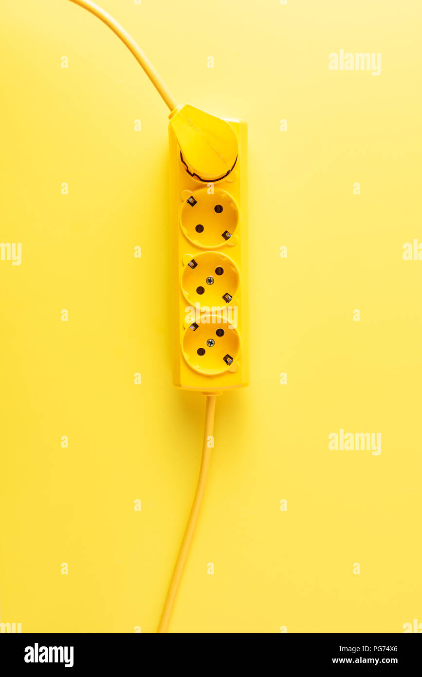 top view of bright yellow socket outlet with plug on yellow background ...