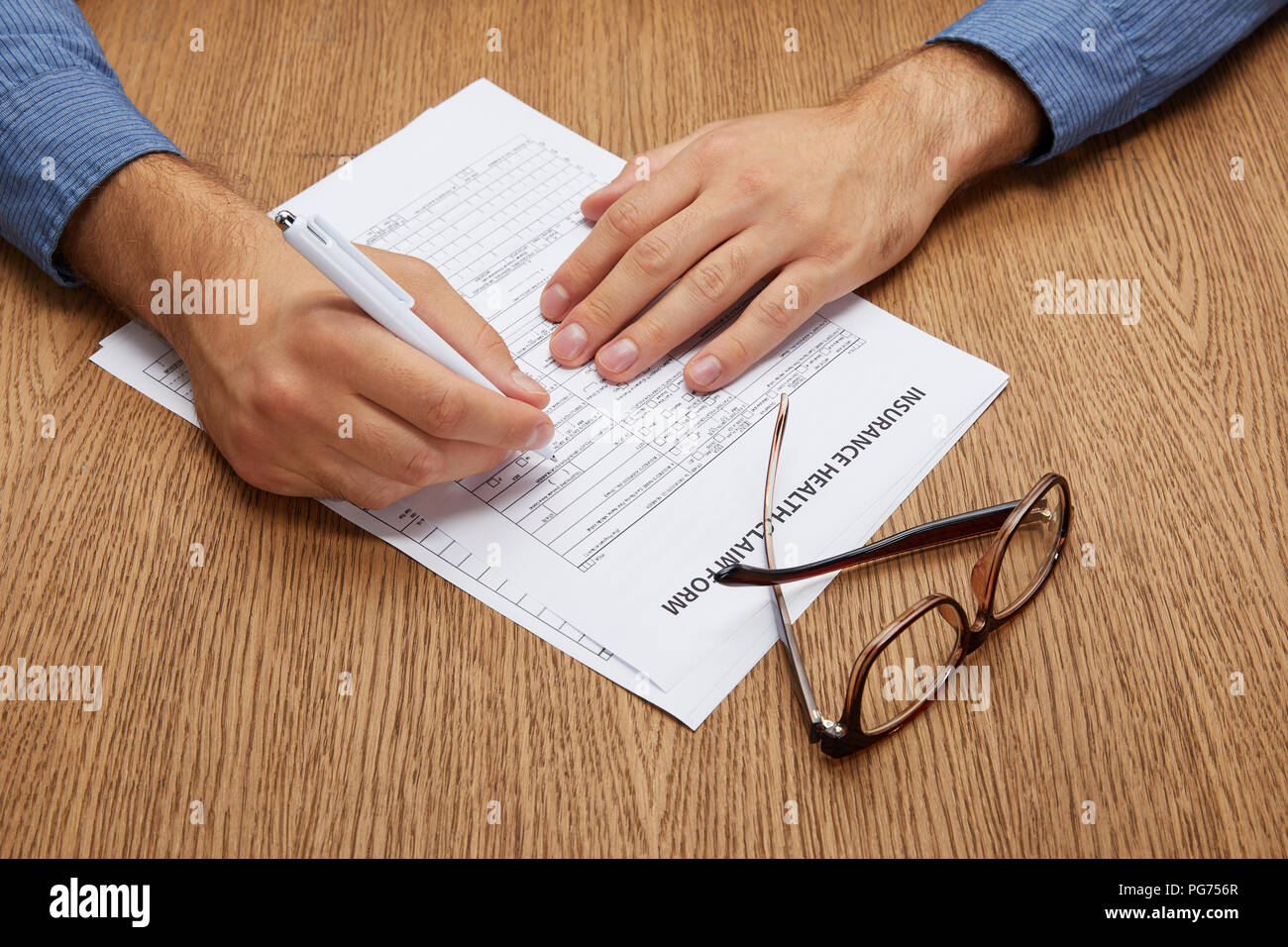 close-up partial view of person signing insurance form at wooden table ...