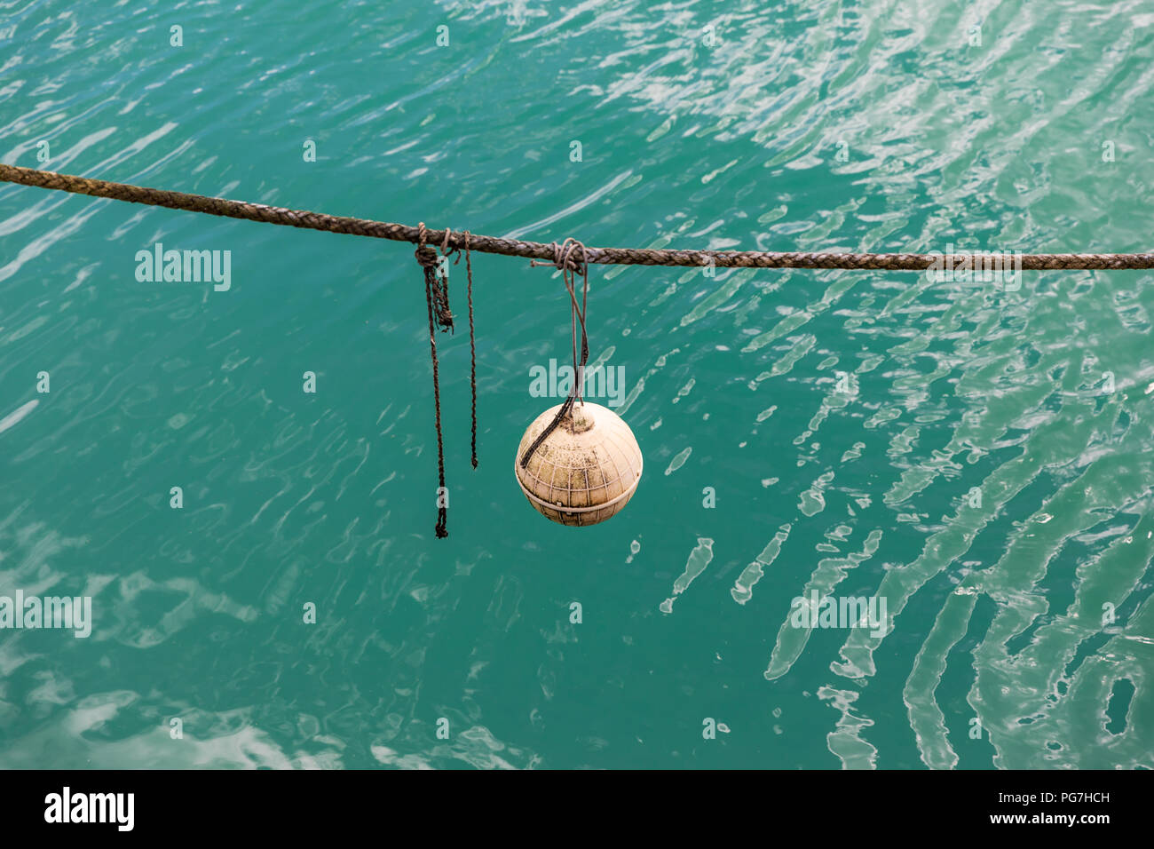 Buoy hanging on a rope over green water; Toya Harbour, Yomitan, Okinawa ...