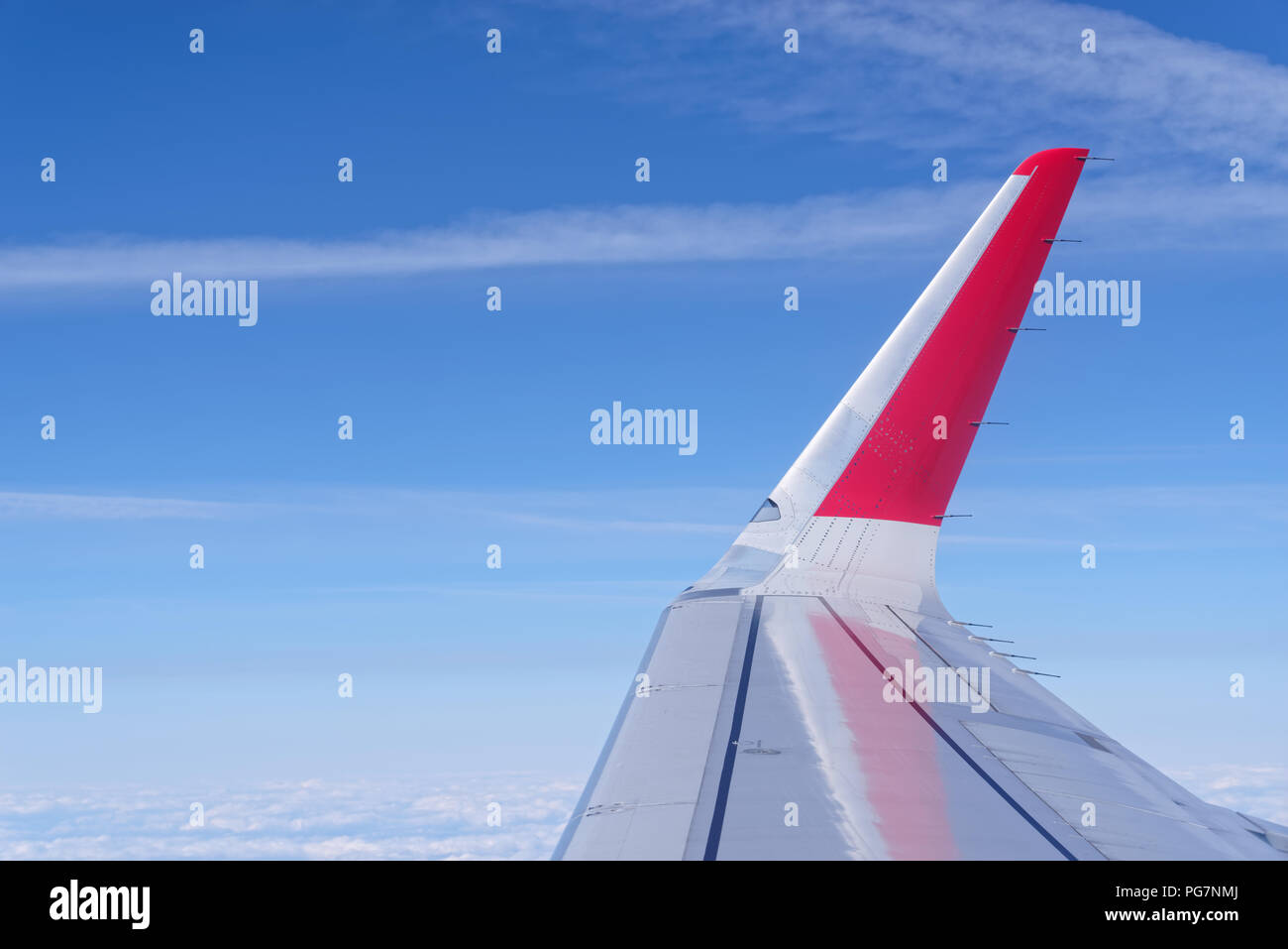 Airplane wing with red colored winglet against blue sky. View from ...