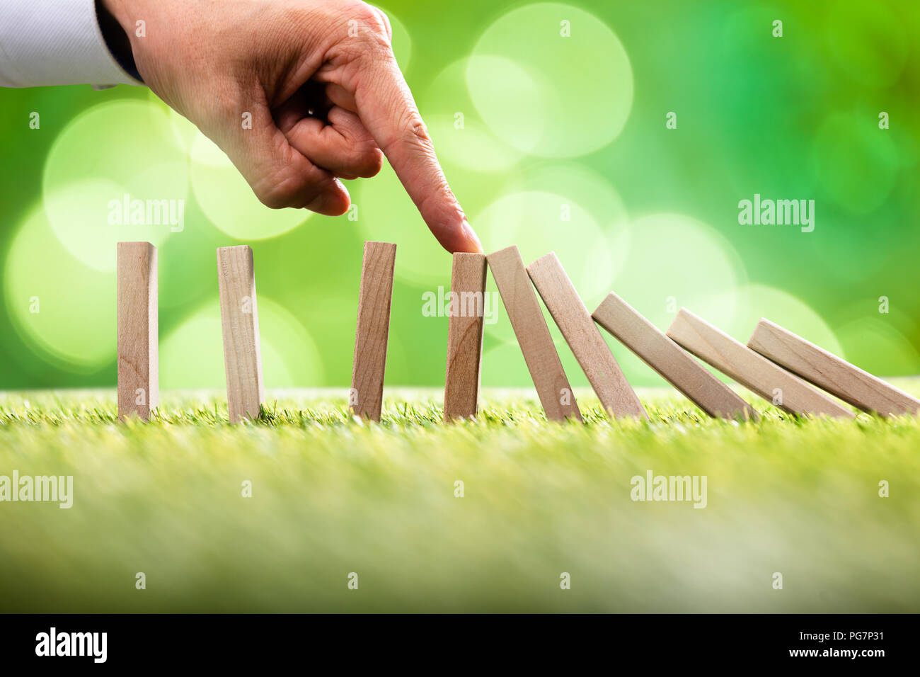 A Person's Hand Stopping Falling Wooden Blocks On Green Grass Stock ...