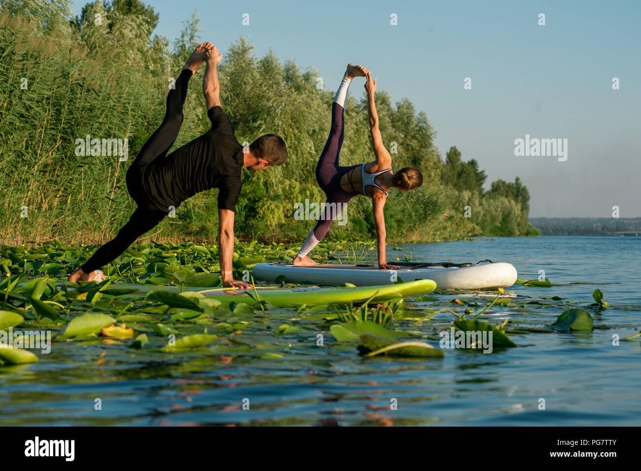 stand up paddle board yoga performed by beautiful couple on the bright ...