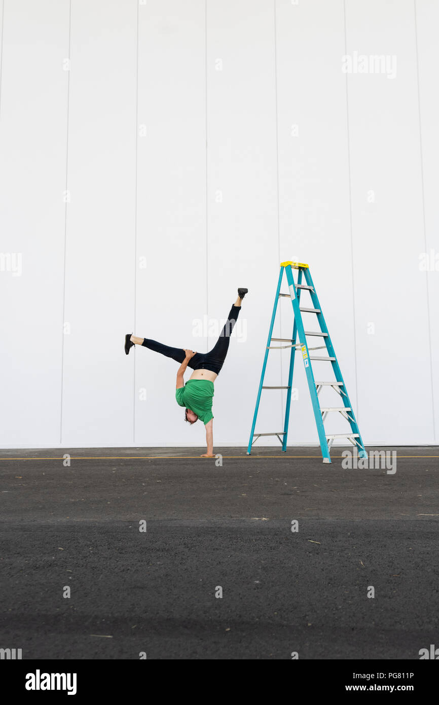 Acrobat training one-armed handstand next to ladder Stock Photo - Alamy