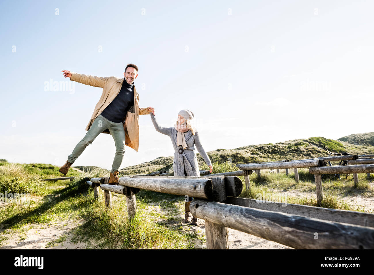 Woman helping man balancing on wooden stakes in dunes Stock Photo - Alamy