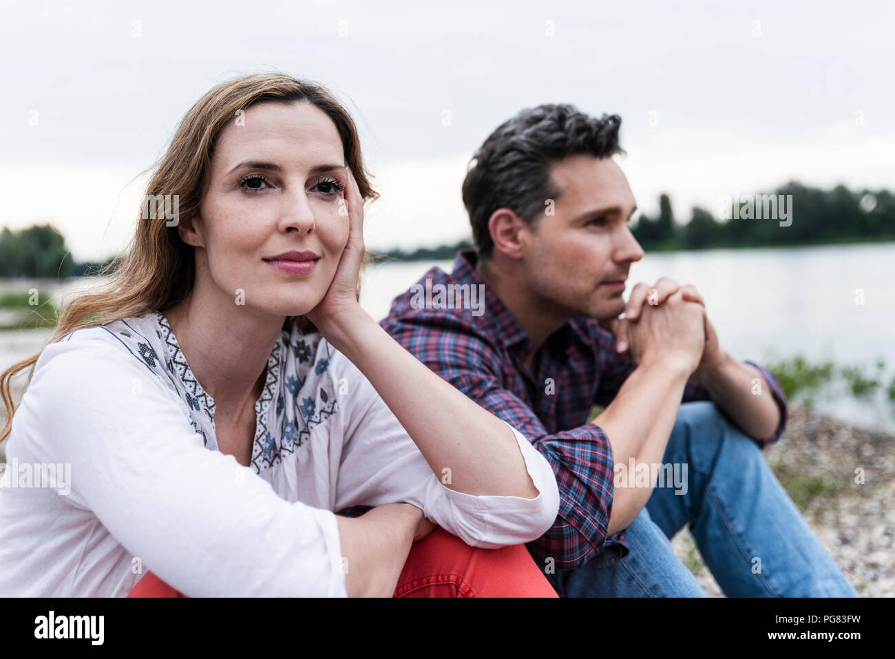 Couple sitting at the riverside thinking Stock Photo - Alamy