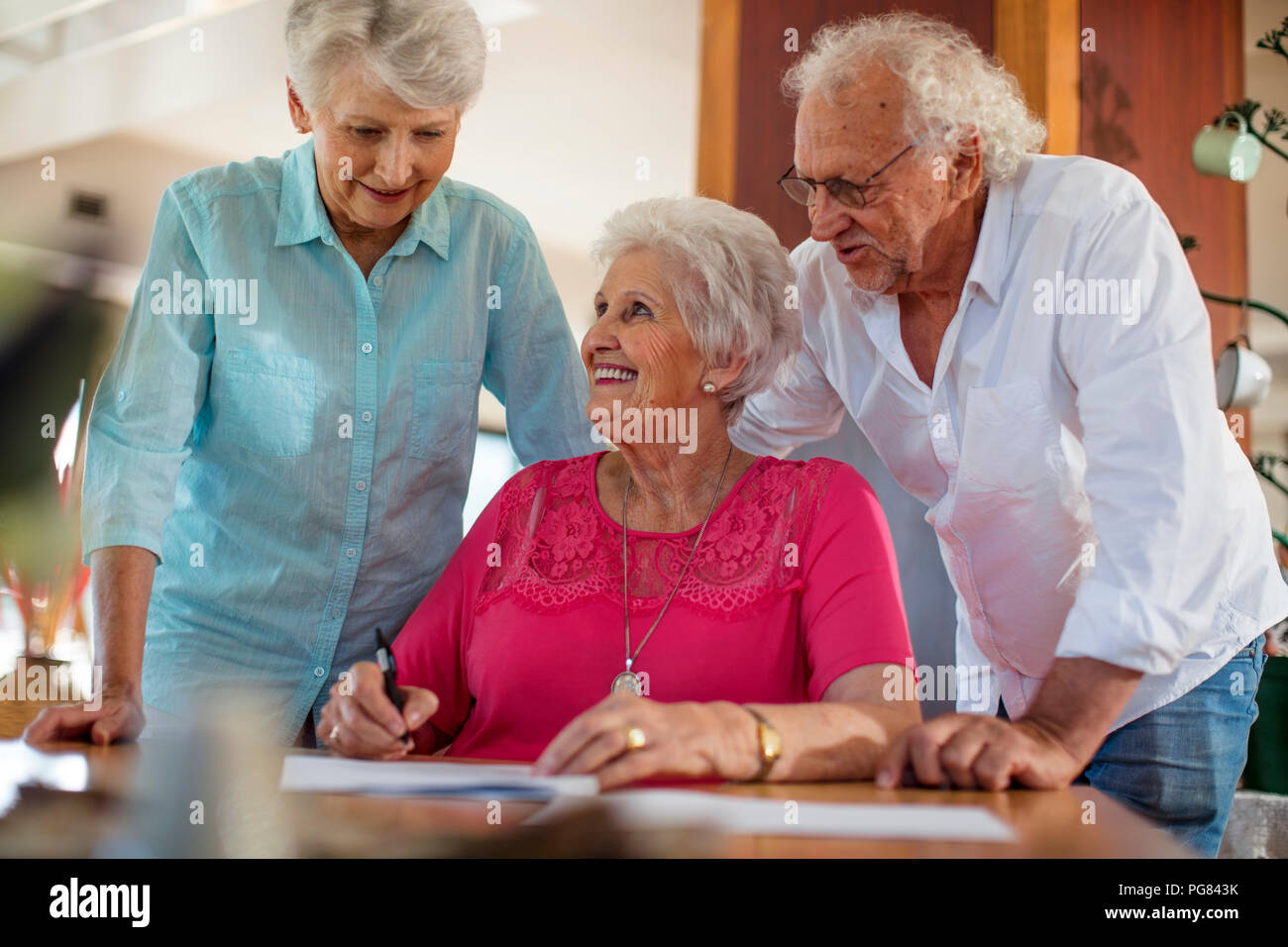 Senior woman signing a contract, friends reassuring her Stock Photo - Alamy
