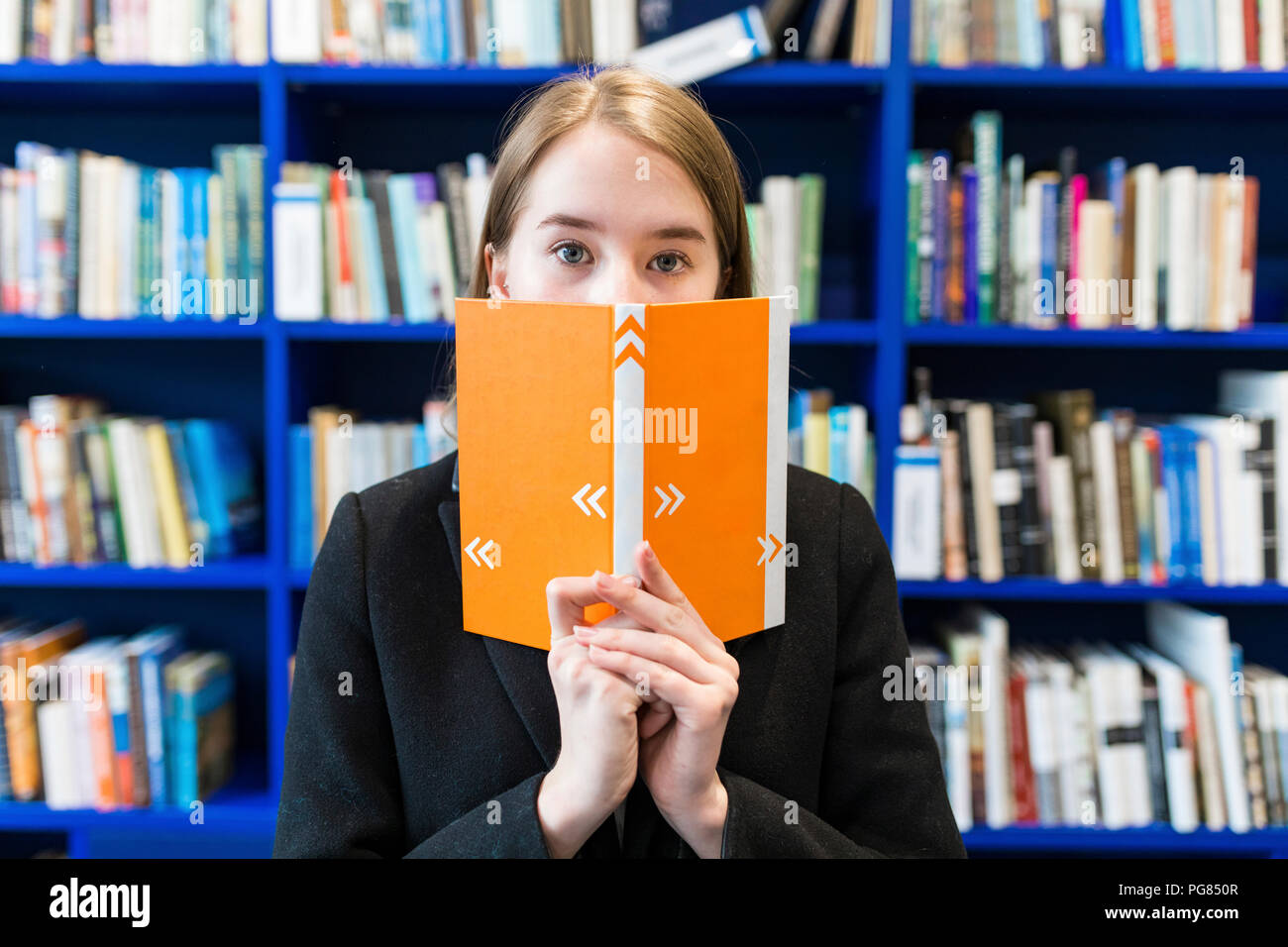 Teenage girl hiding behind book in a public library Stock Photo - Alamy