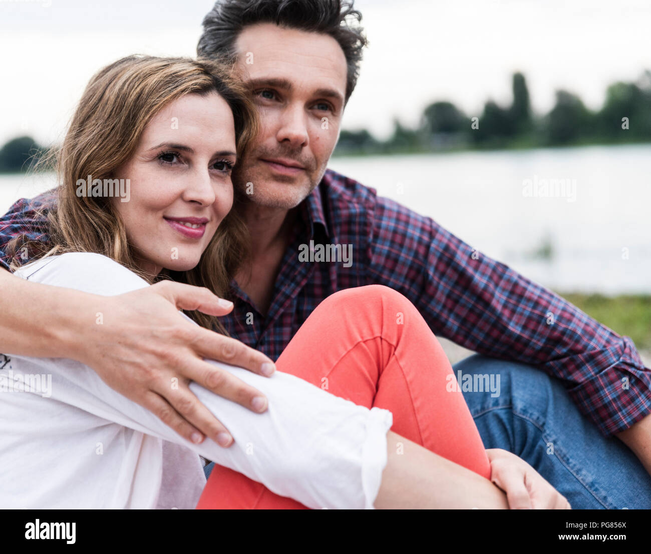 Affectionate happy couple sitting at the riverside Stock Photo - Alamy
