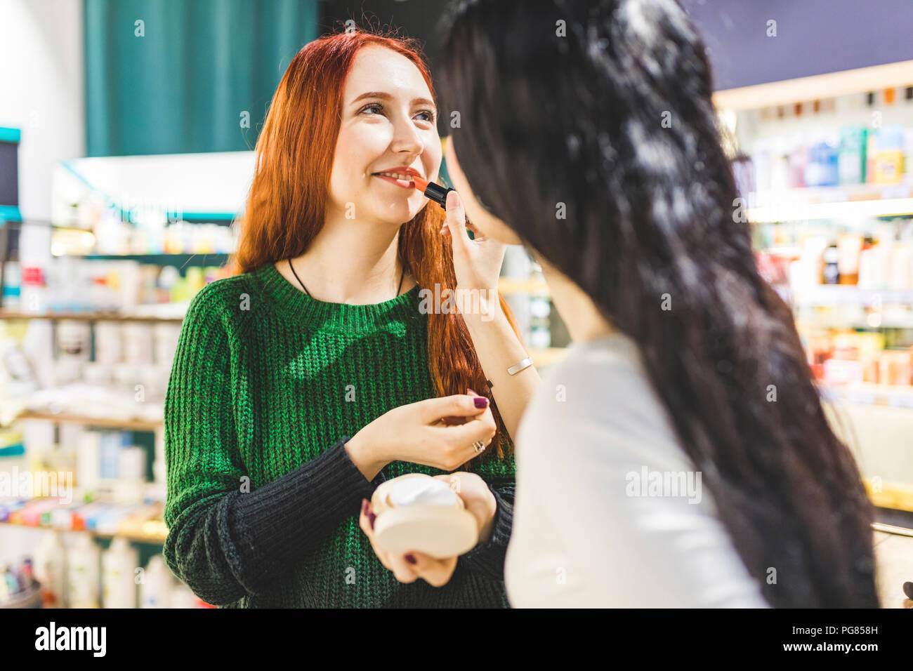 Two women in a cosmetics shop trying lipstick Stock Photo - Alamy