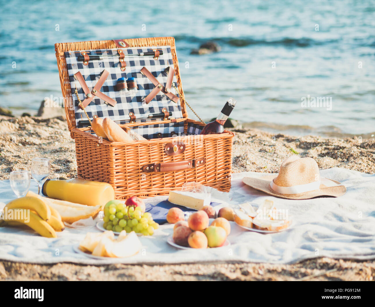 Closeup of picnic basket with drinks, wine, fruits on sand beach near ...