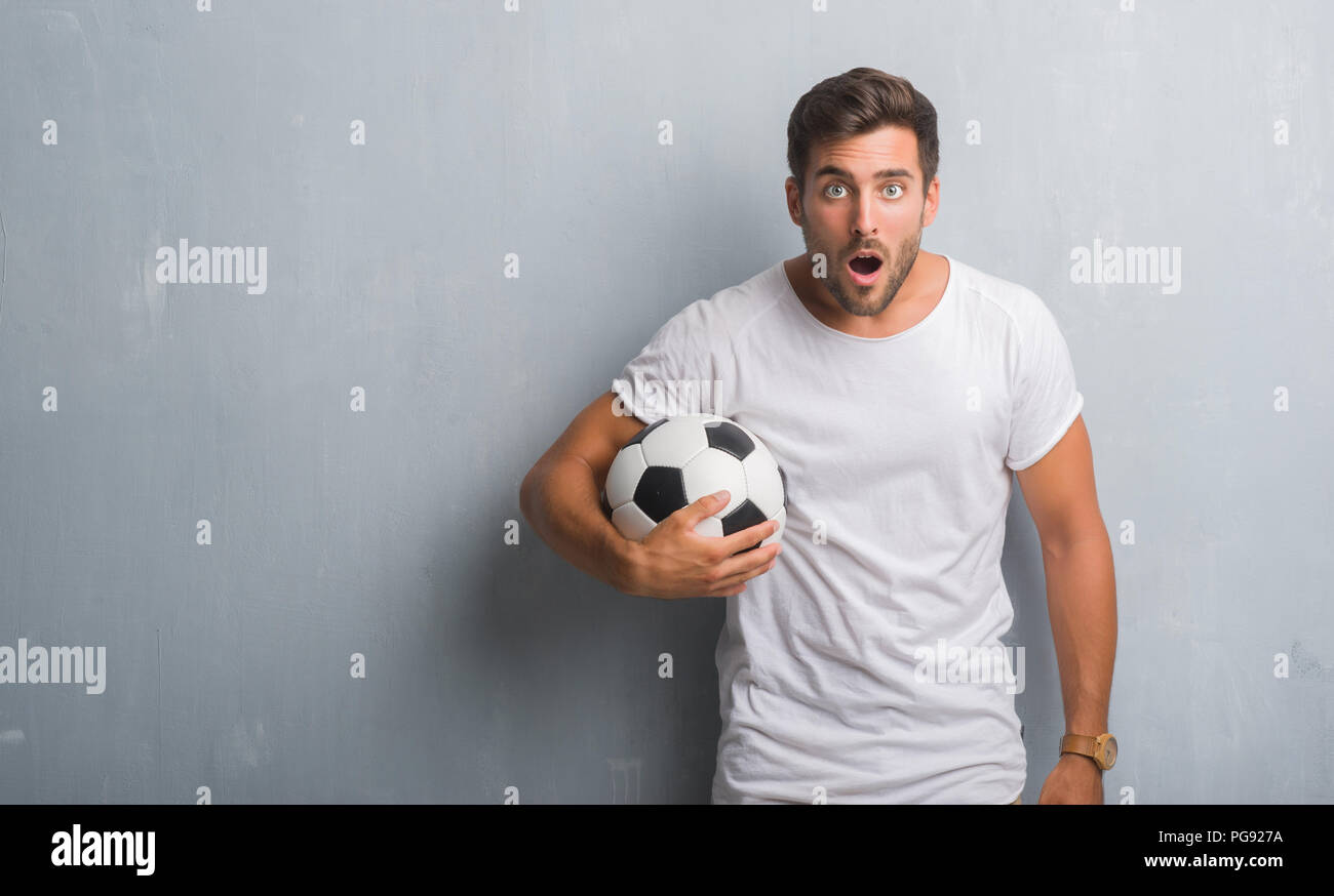 Handsome young man over grey grunge wall holding soccer football ball ...