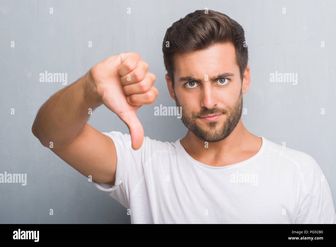 Handsome young man over grey grunge wall with angry face, negative sign ...
