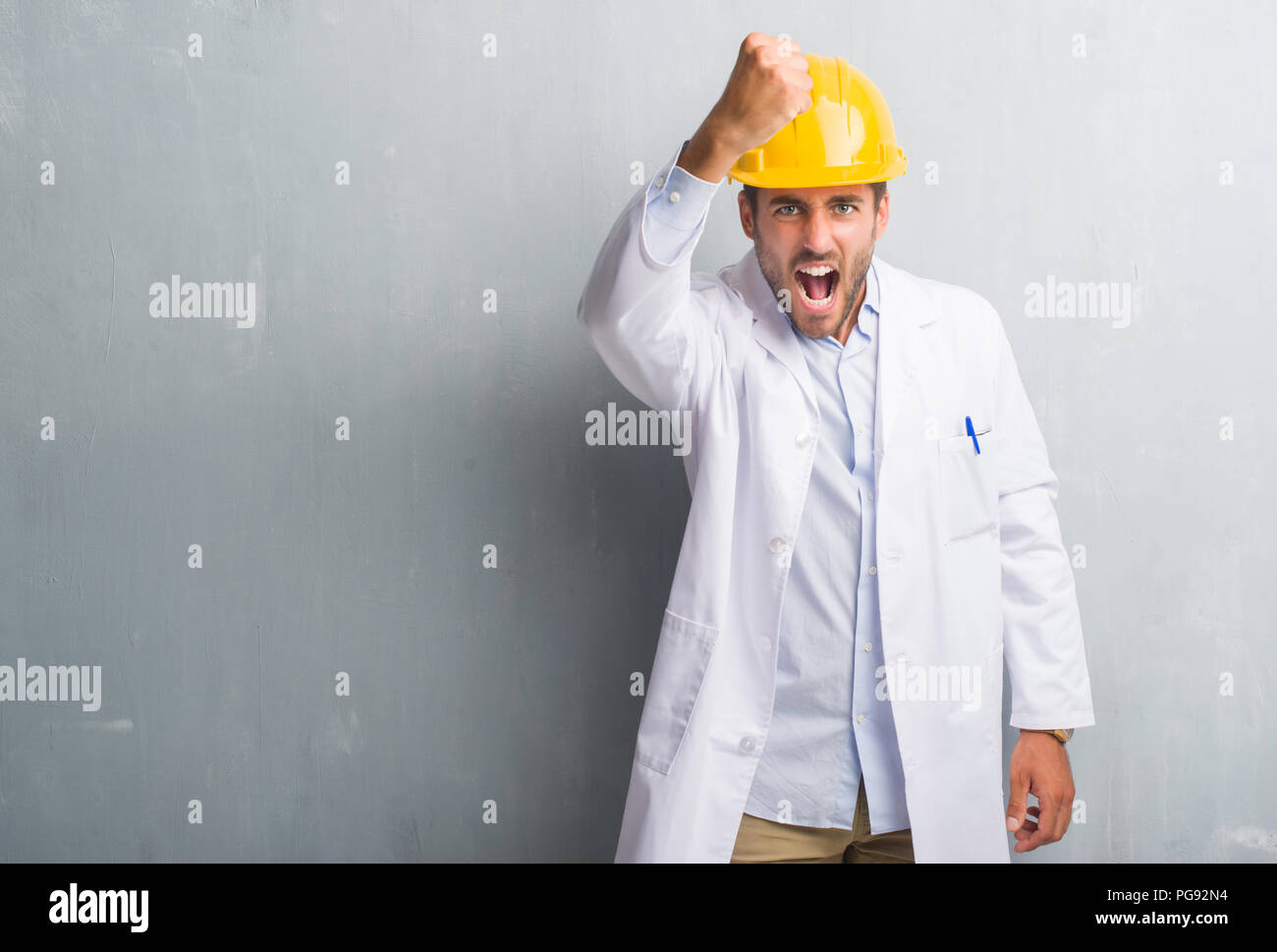 Handsome young engineer man over grey grunge wall wearing safety helmet ...