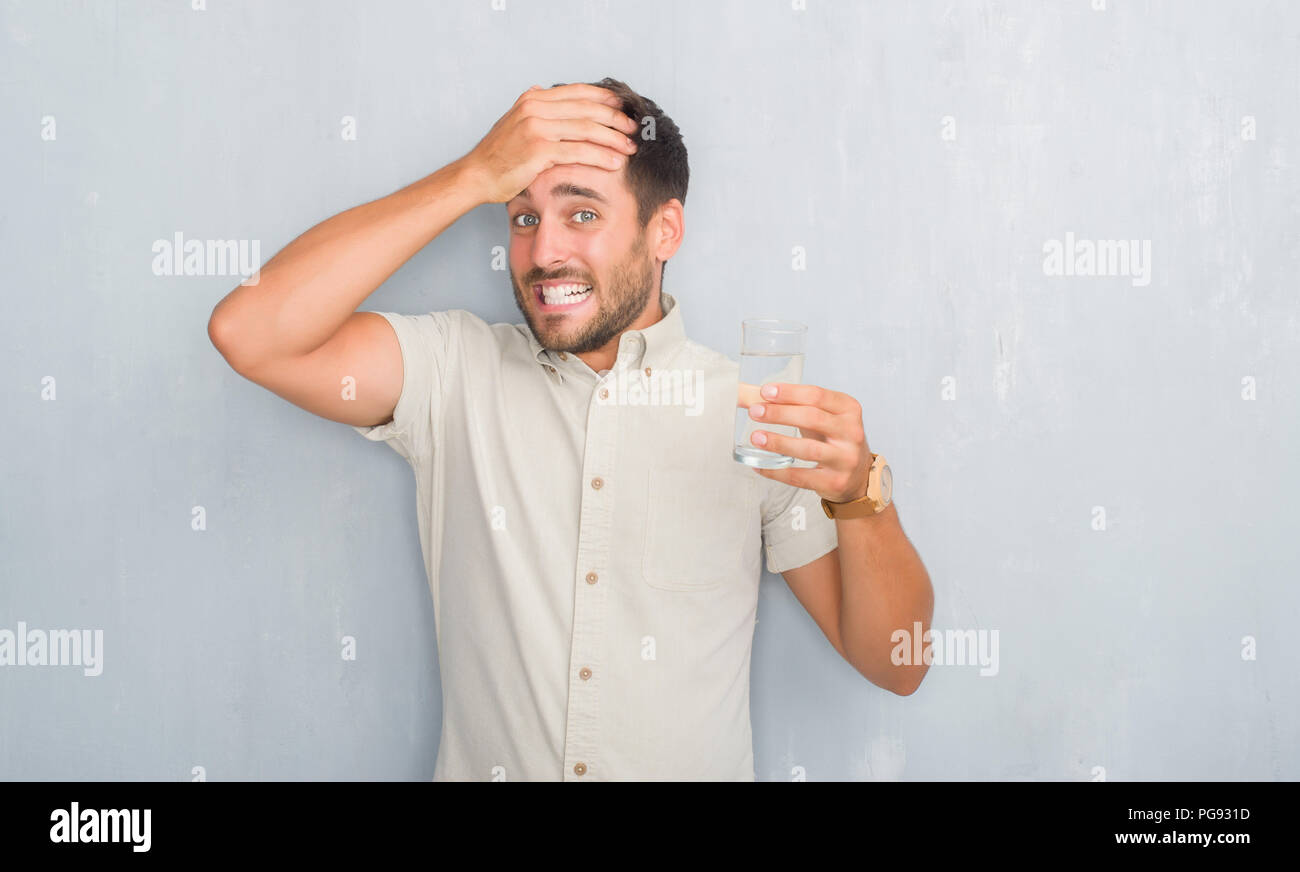 Handsome young man over grey grunge wall drinking glass of water ...