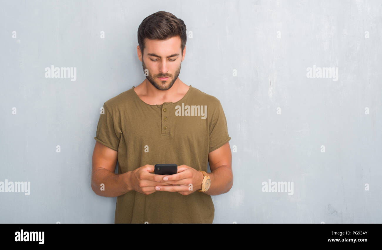 Handsome young man over grey grunge wall texting a message using ...